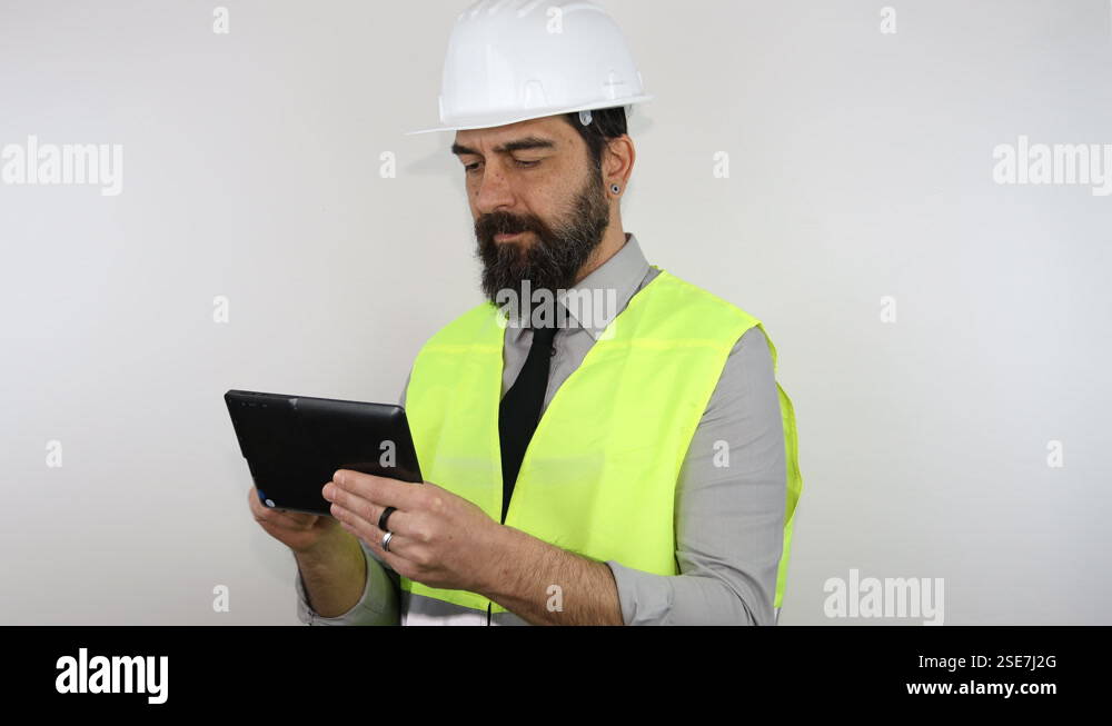 Engineer wearing work helmet and reflecting jacket, typing on tablet ...
