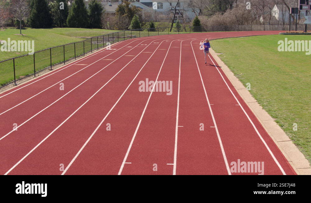 Teen girl on a track breaks into a run towards and past camera on a ...