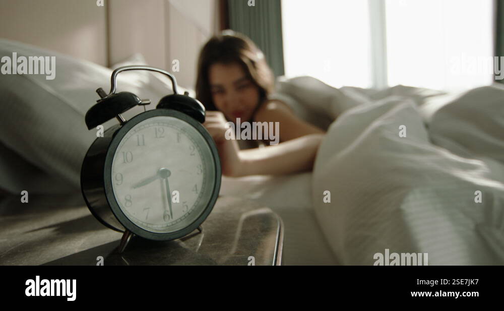 Young girl setting off ringing alarm clock and getting up from sleep in ...