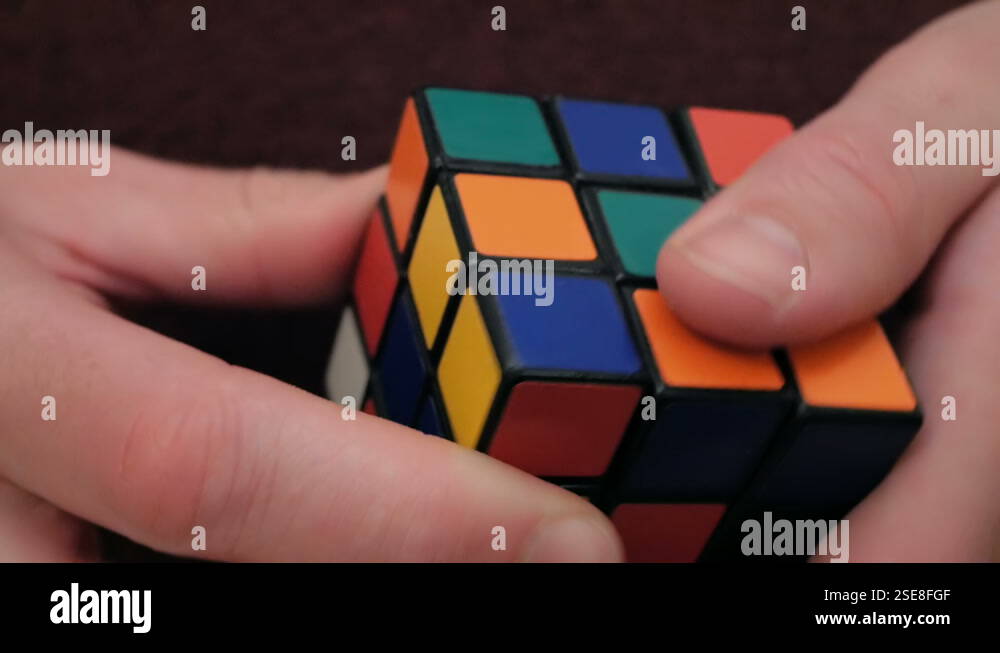A young attractive guy collects a rubik's cube. Close-up of a young man ...