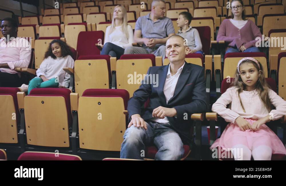 Interested adults with tween children absorbedly watching film in movie ...
