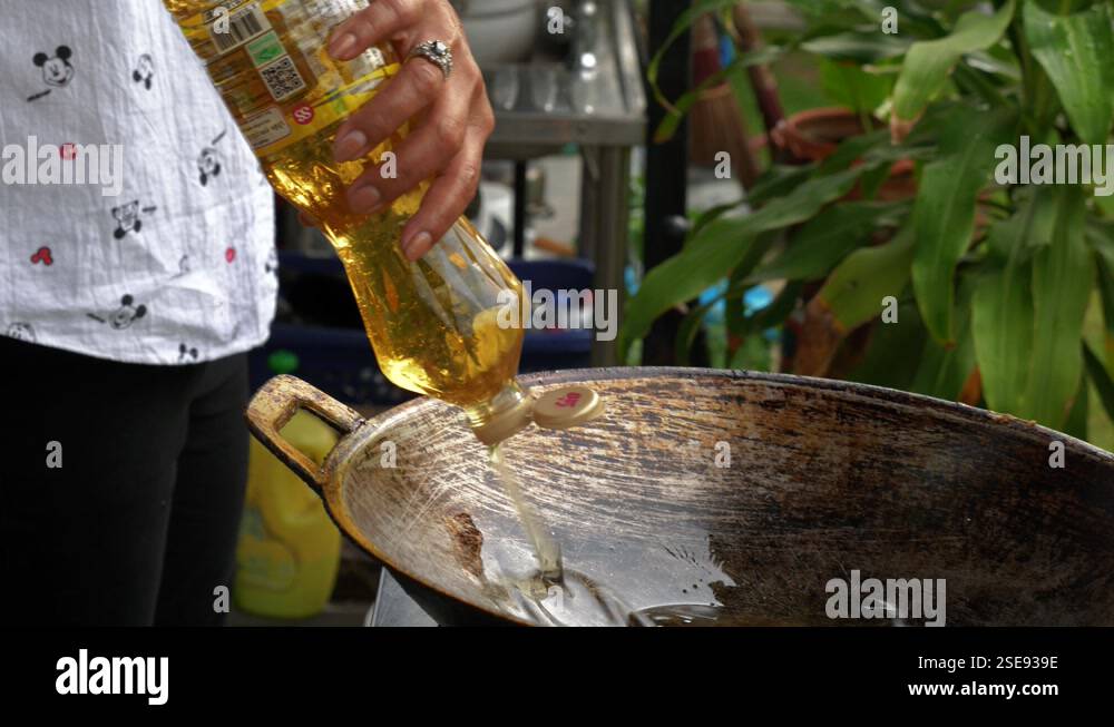 Person pouring oil into wok style pan directly from plastic bottle ...