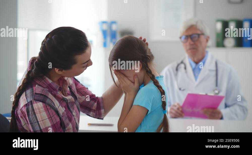 Portrait of mother comforting cute little girl crying at doctor office ...