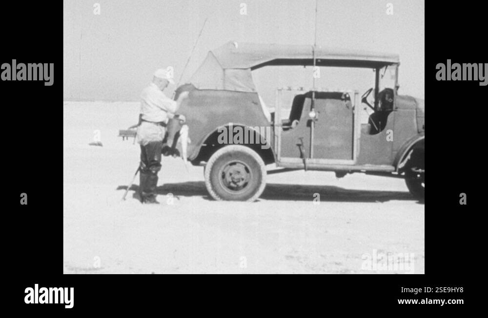 1940s: Man carries freshly caught fish to jeep parked on beach of ocean ...