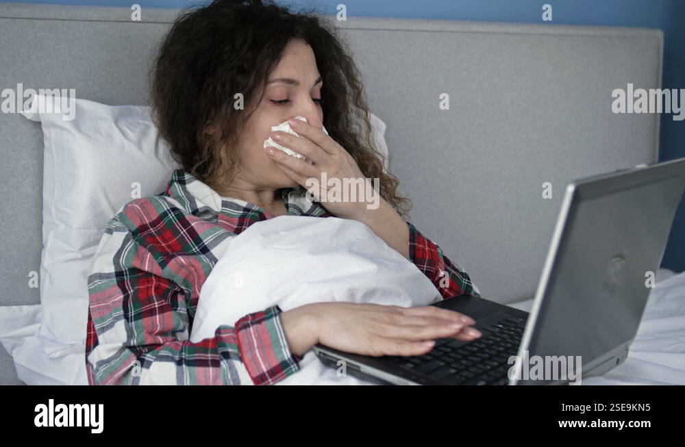Sick woman lying in bed with laptop computer and smartphone in self ...