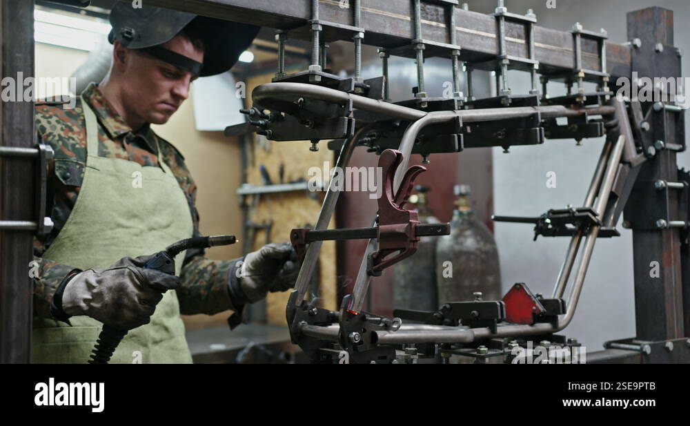 A young man welds iron parts stops and looks at the welding continues ...