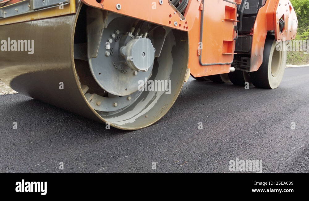 Road construction. Asphalt compactor heavy machine working on a fresh ...