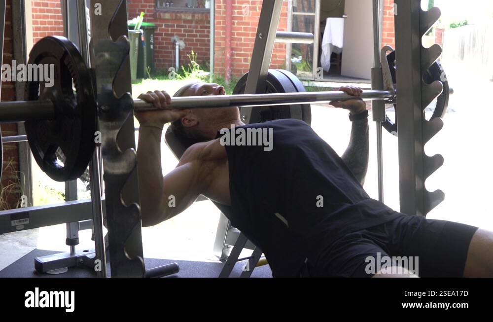 Muscly man in home gym exercising dooing incline barbell bench press ...