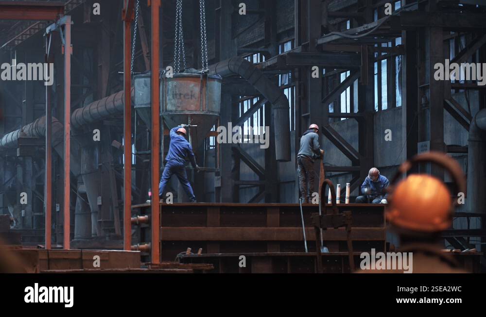 Steel workshop workers clean mold and container from sludge in foundry ...
