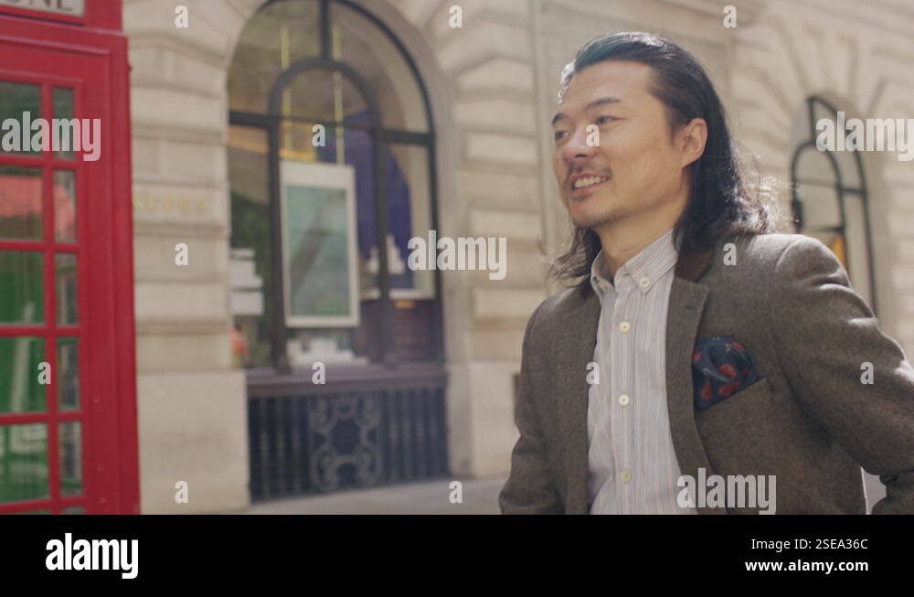 Handsome Asian business man using his phone as he walks through the ...