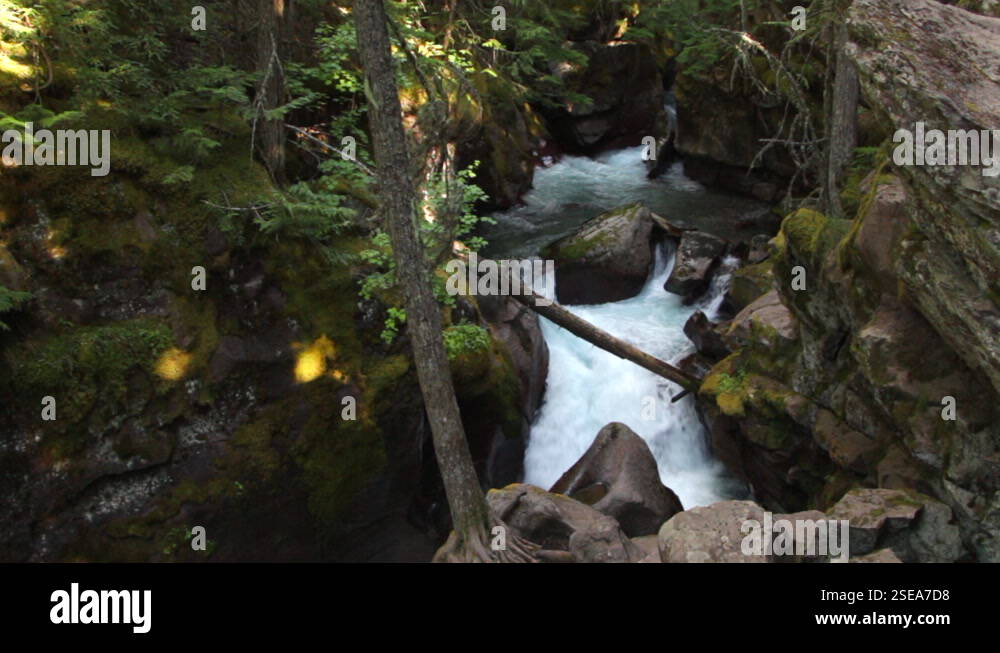 Rough foamy waterfall flowing through rocky moss layered boulder in an ...