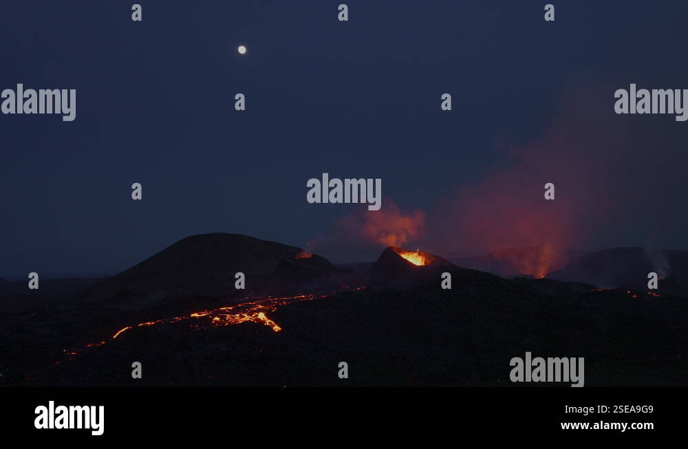 Wide shot showing spewing volcano with magma during dark night and full ...