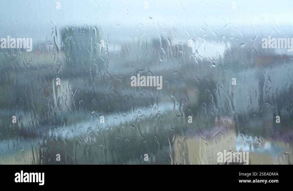 Window with dripping rain drops close-up with a blurry city in the ...