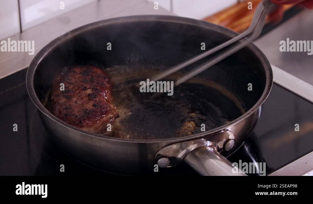 Restaurant kitchen - the chef is frying a steak in a deep pan and turns ...