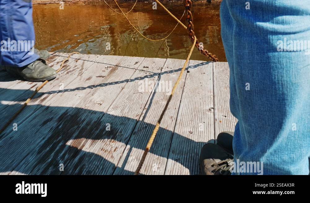 Legs of two men onboard of tug who put big chain into water to fix it ...