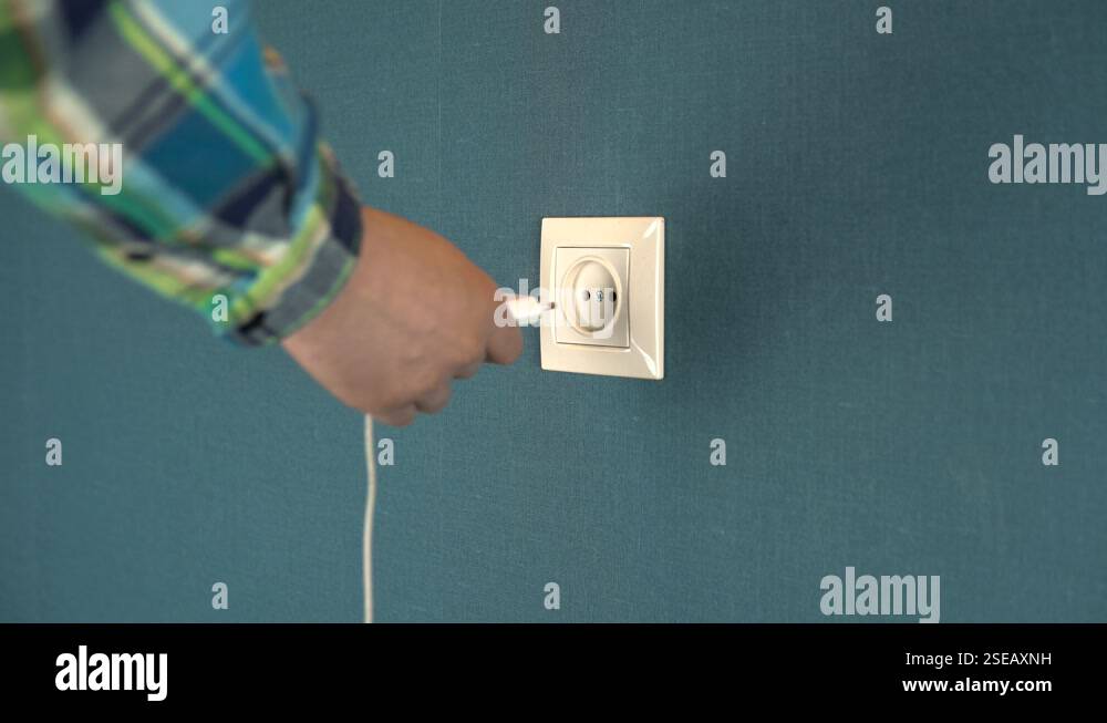 A man plugs a phone charger into a wall outlet. Rosette in the wall ...
