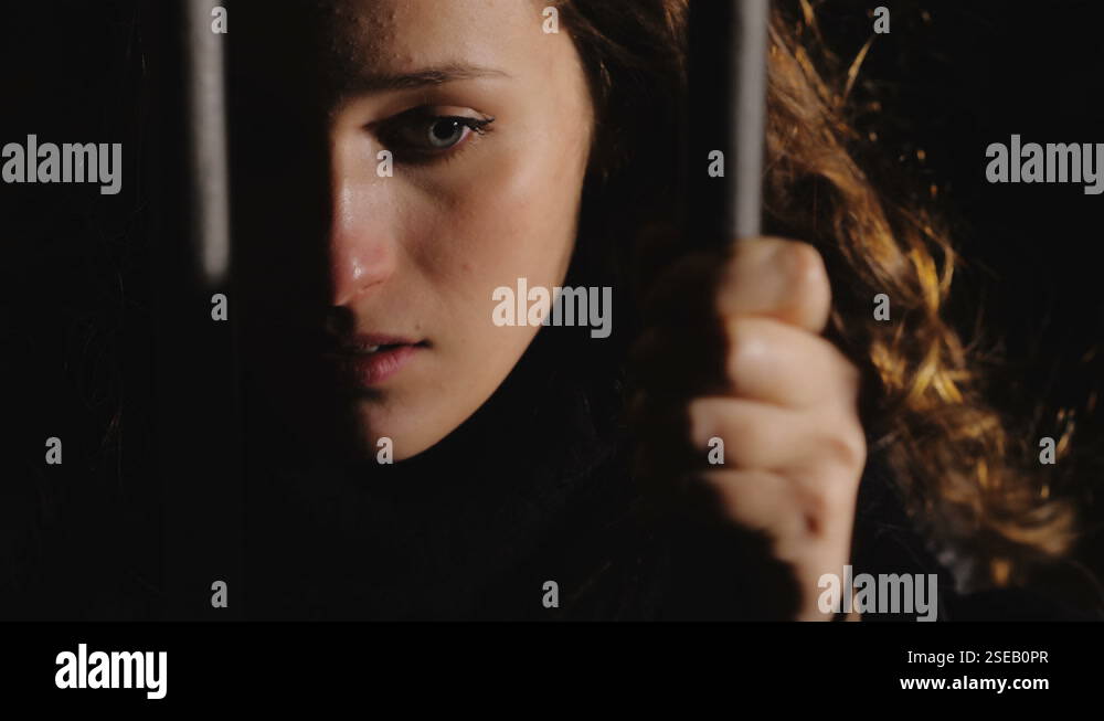 symbol of restriction - sad girl behind the bars of a gate in the dark ...