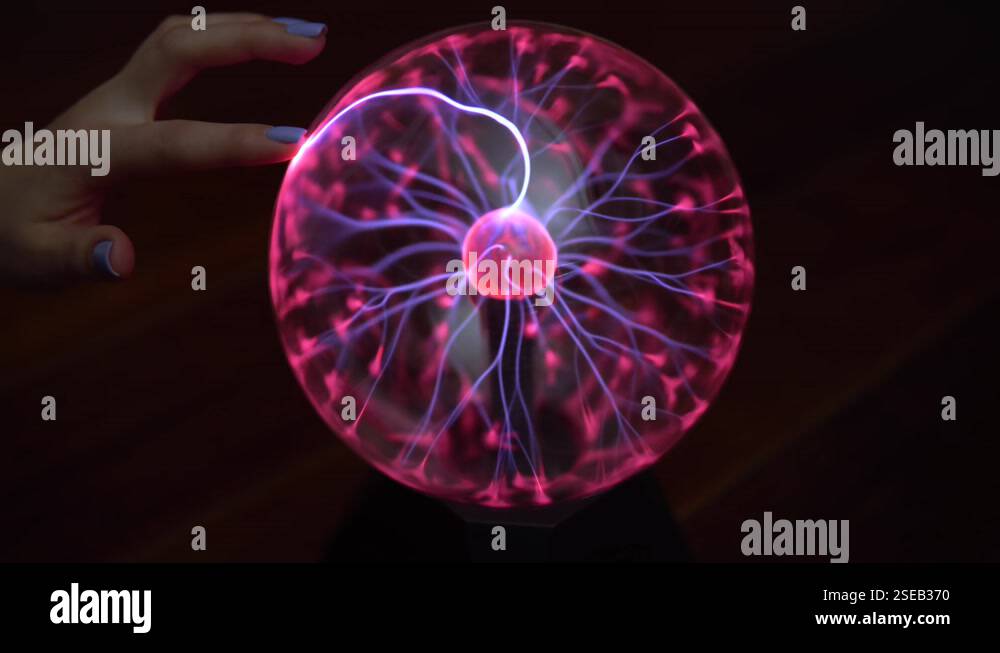 A female hand touches a plasma ball giving out small lightning bolts ...
