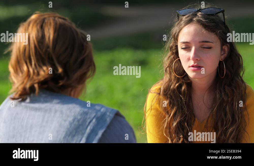 confide in the park - young woman sitting at park confides in a friend ...