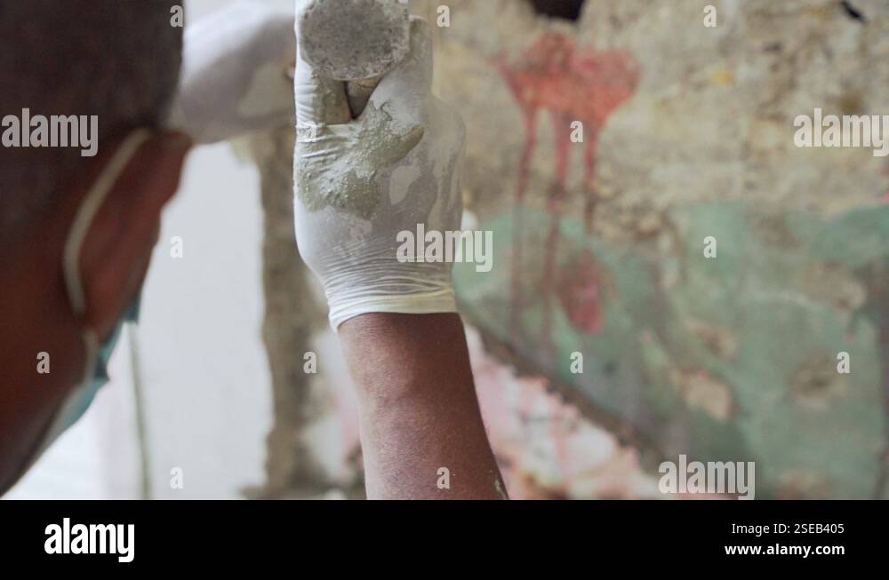 Back view of unrecognizable bricklayer removing plaster from wall ...