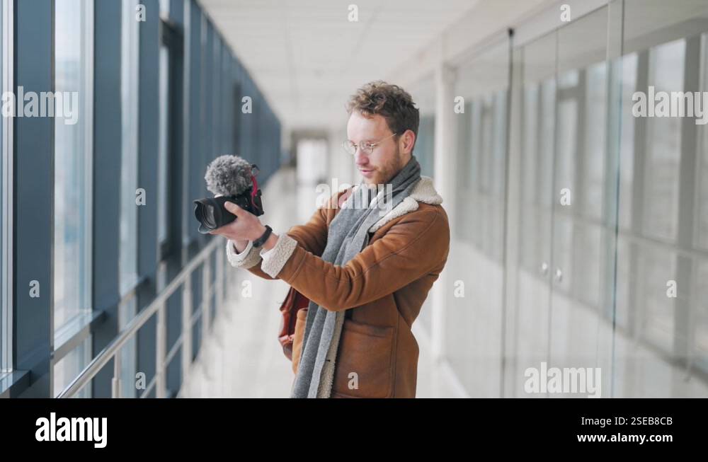 Stylish man with a mirrorless camera filming a blog in the hallway of a ...