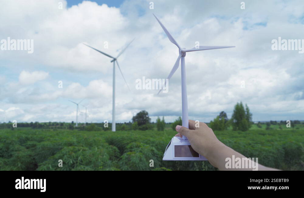 People hand holding a wind turbines model or windmills farm field ...