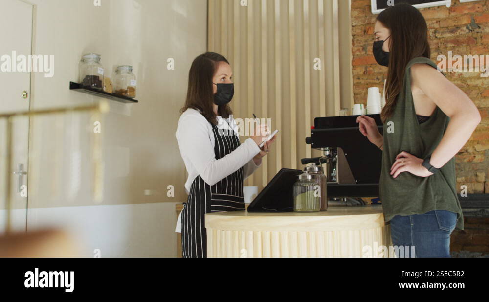 Caucasian waitress wearing face mask taking order from caucasian female ...