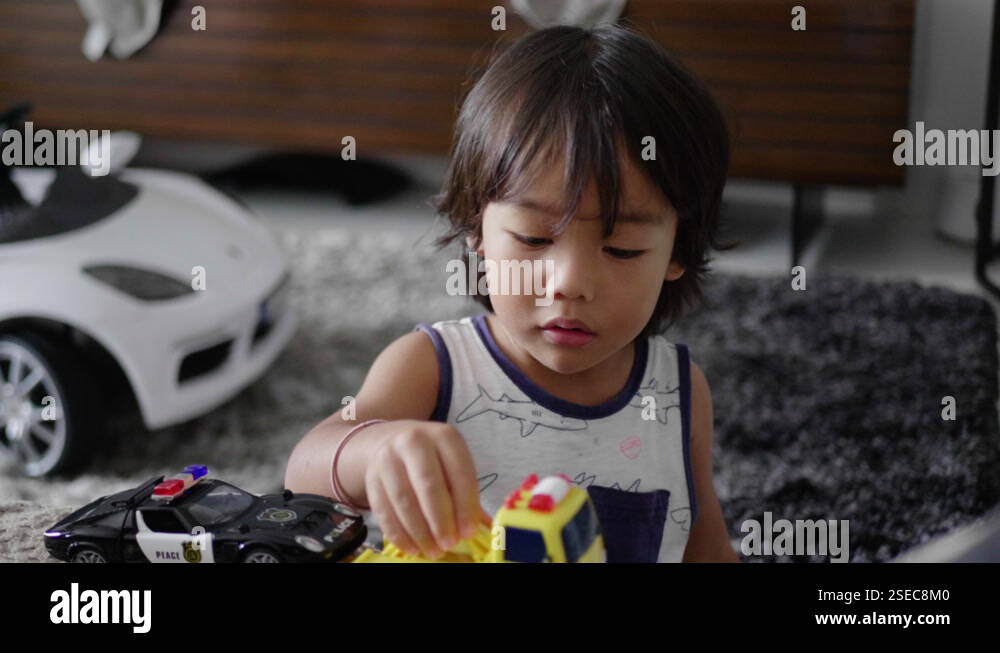 Asian boy playing with his police car and toy truck and is distracted ...