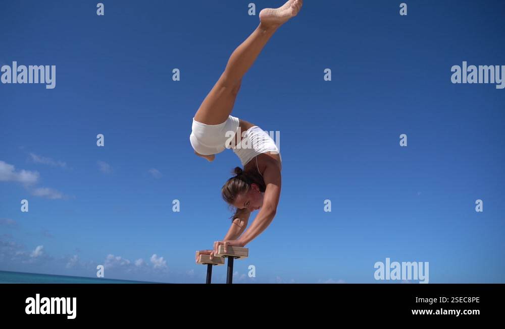 Woman wearing white doing handstand on the beach with sea ...