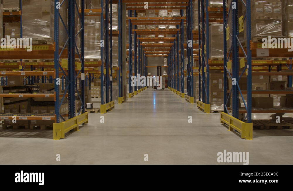 Distant forklift turning around corner in long corridor of logistical ...
