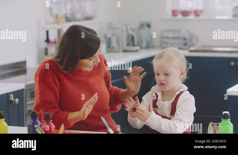 Daughter Showing Mother Messy Hands As They Paint Picture In Kitchen ...