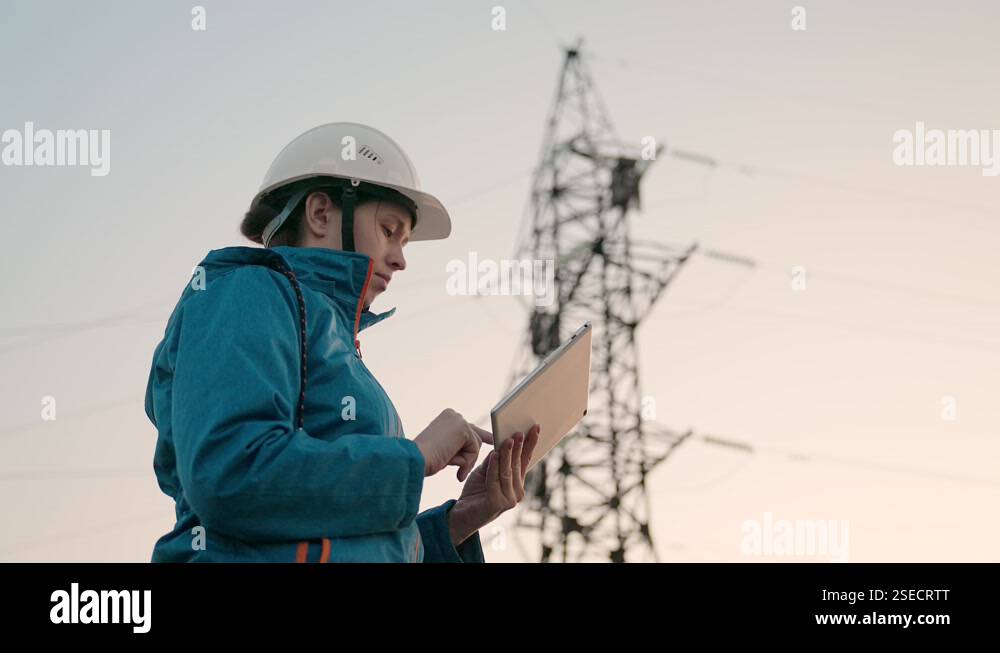 A woman power engineer in white helmet inspects power line using data ...