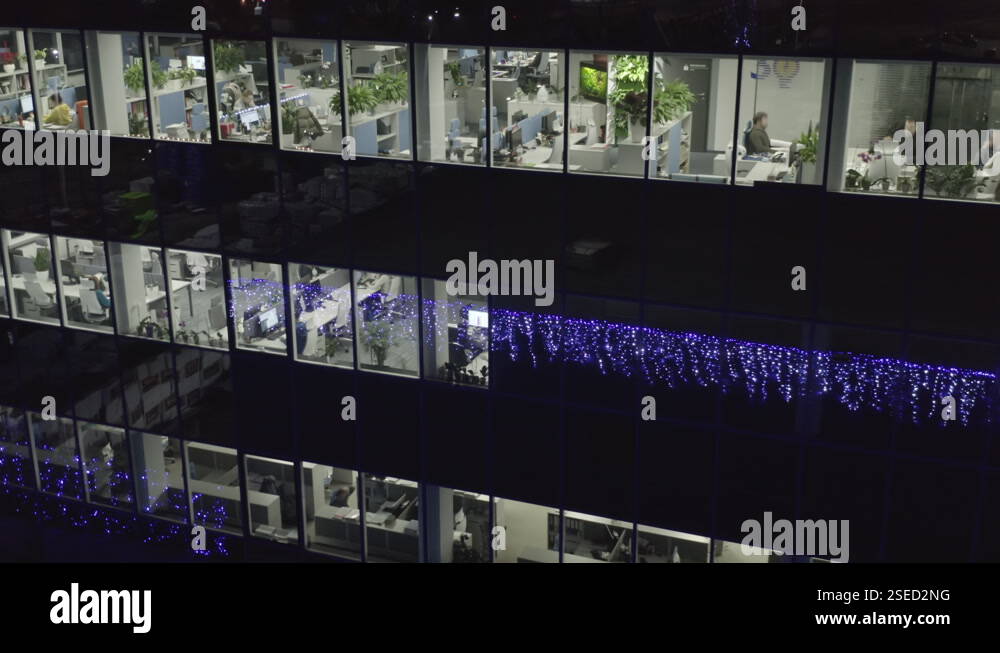 Office windows of a glazed skyscraper glow at night with city lights ...