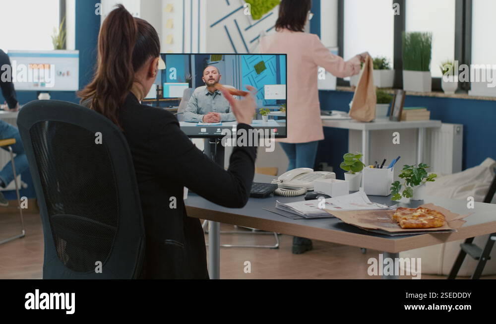 Executive manager eating pizza slice discussing with remote collegue ...