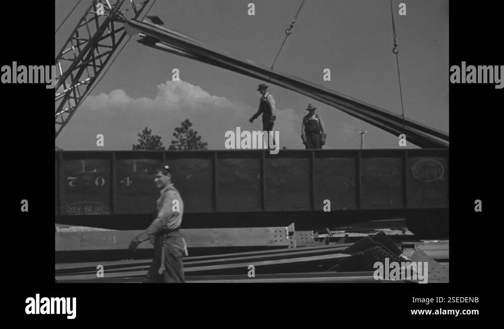 1940s: Workers supervise as a crane lifts steel girders from a ...