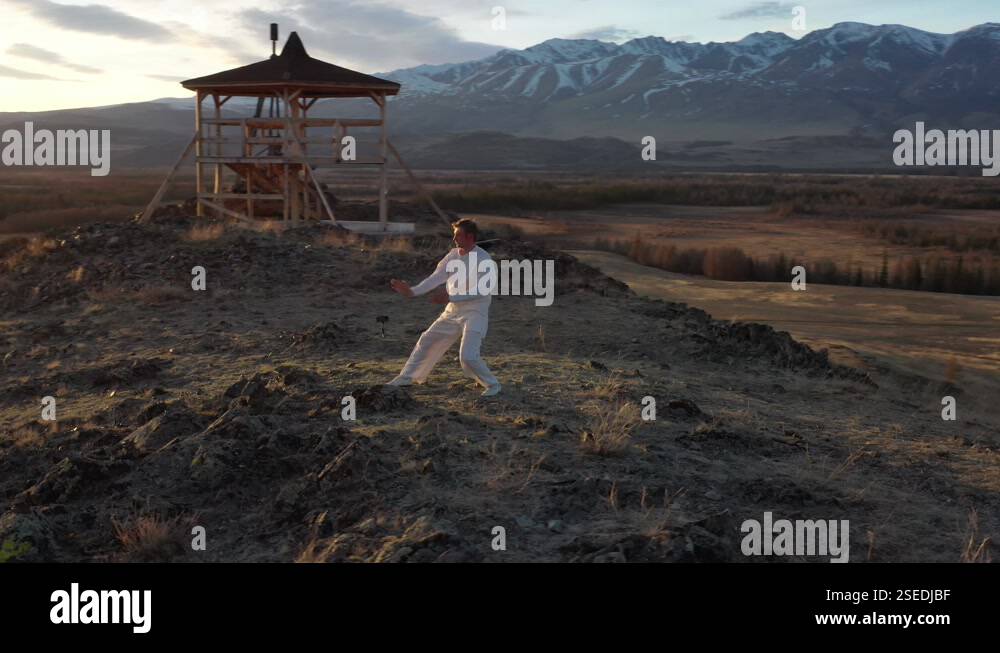 Video of wushu master in a white uniform training on the hill on Sun ...