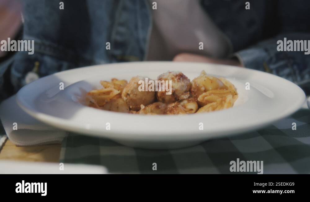 A girl in a denim jacket eats Italian pasta with beef mitbols and ...
