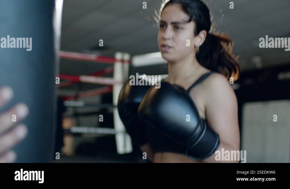 Boxing, woman fighter trains her punches, beats a punching bag ...