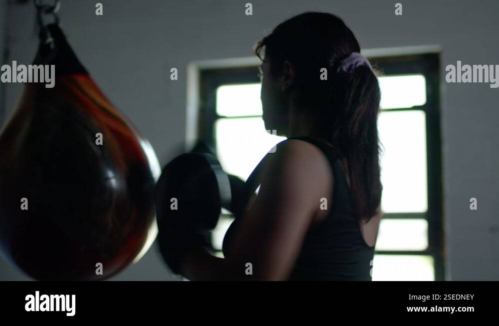 Boxing, woman fighter trains her punches, beats a punching bag ...
