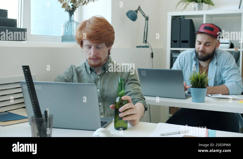 Drunk man holding beer bottle and drinking working with laptop then ...