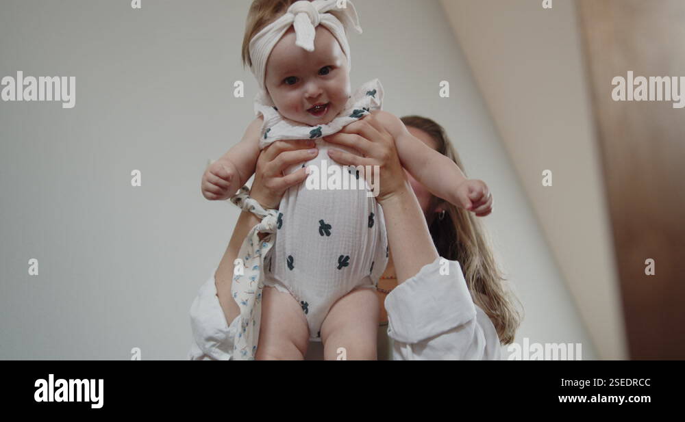 Young mother lifts up her cute baby daughter having fun and laughing ...