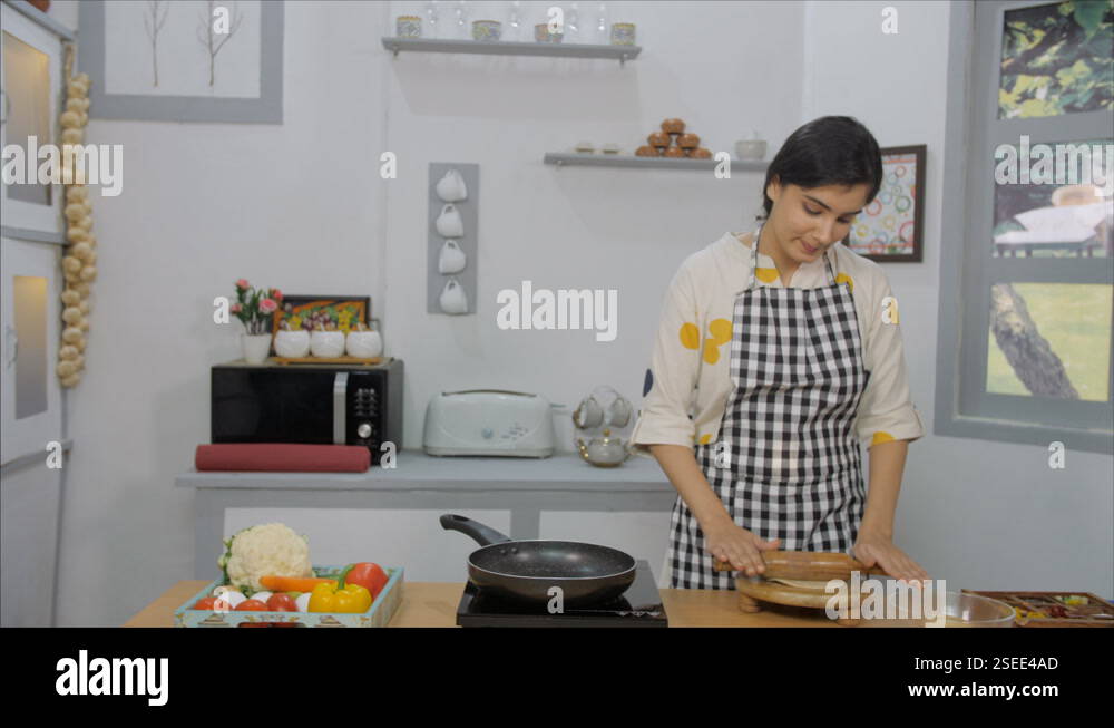 A young lady making chapati (Indian bread) in the kitchen at her home ...
