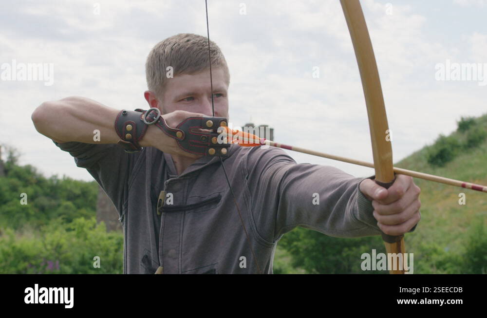 a young guy shoots a bow at a target, in nature, and hits the target ...