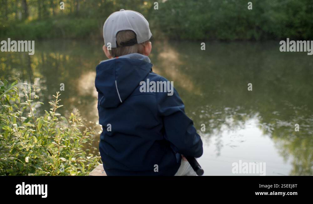 Baby boy fisherman sitting on pier near pond water surface holding fishing rod Stock Video ...