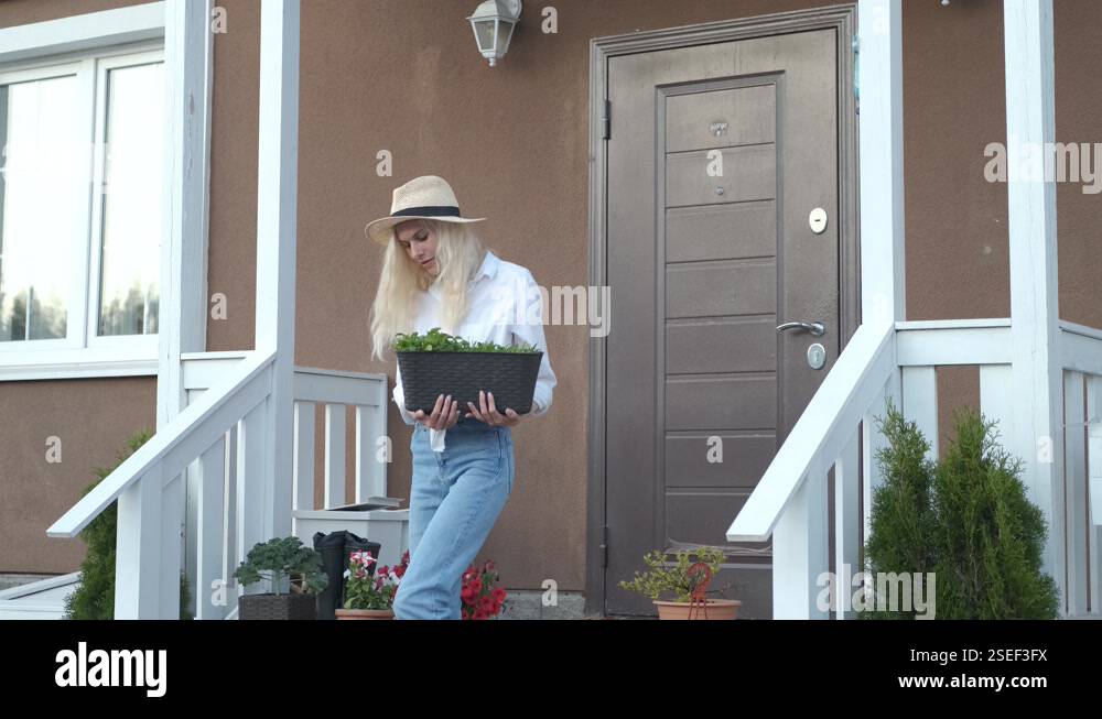 stylish woman gardener walks down the steps of the house with pots with ...