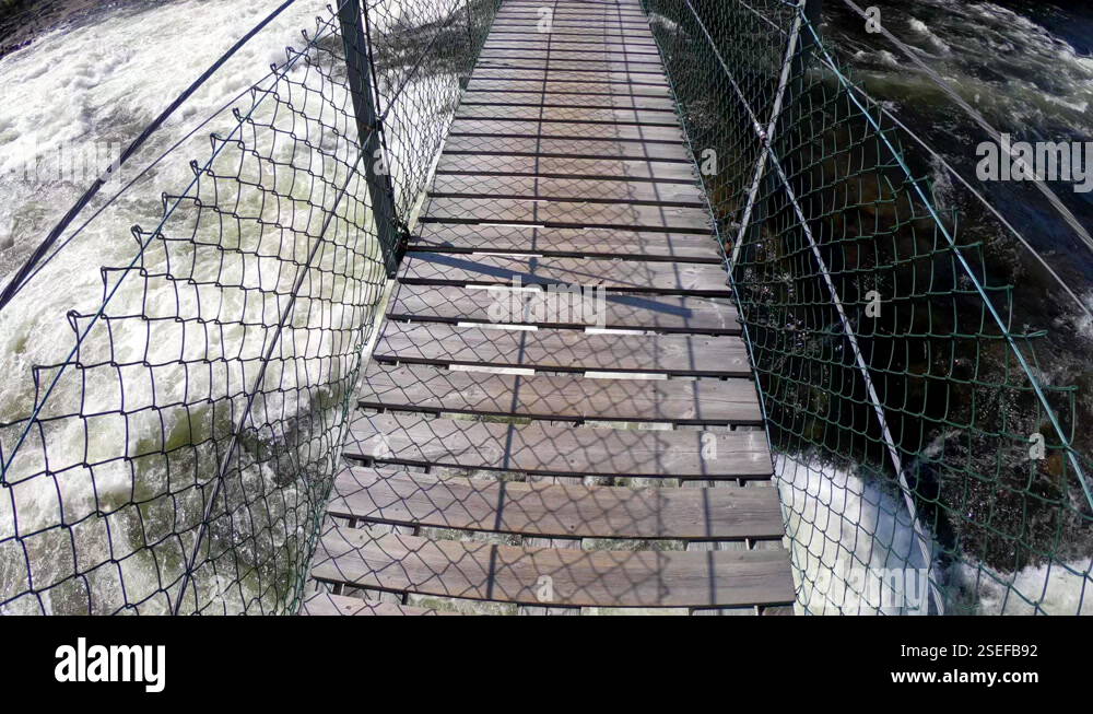 Walking on a suspension bridge over a rippling raging river. Point of ...