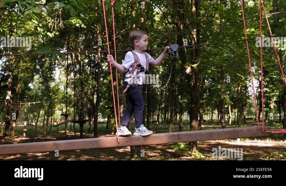 Brave little boy passing the cable route high among trees, adventure ...