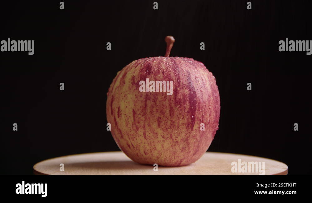 A juicy red apple rotates on a black background. Drops of water on a ...