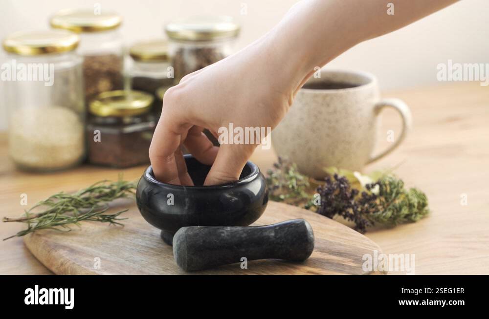 A woman's hand takes dry herbs from a mortar and pours them into a mug ...