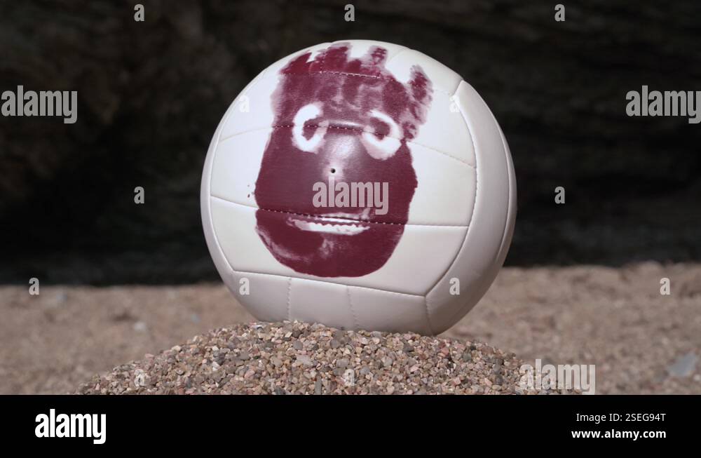 Volleyball ball with face painted on it stands on pile of sand and ...